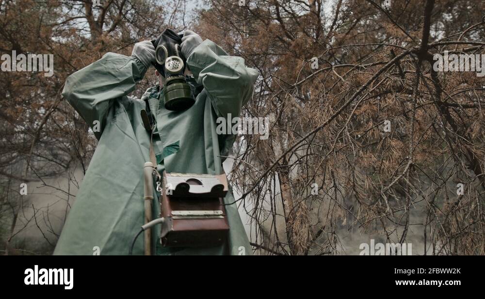 Man wearing a vintage Hazmat suit putting on a WWII gas mask as white ...