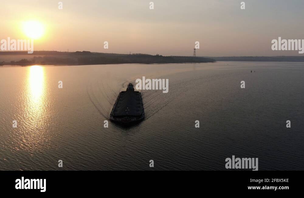 Massive barge with cargo is floating on a river with reflections of the ...