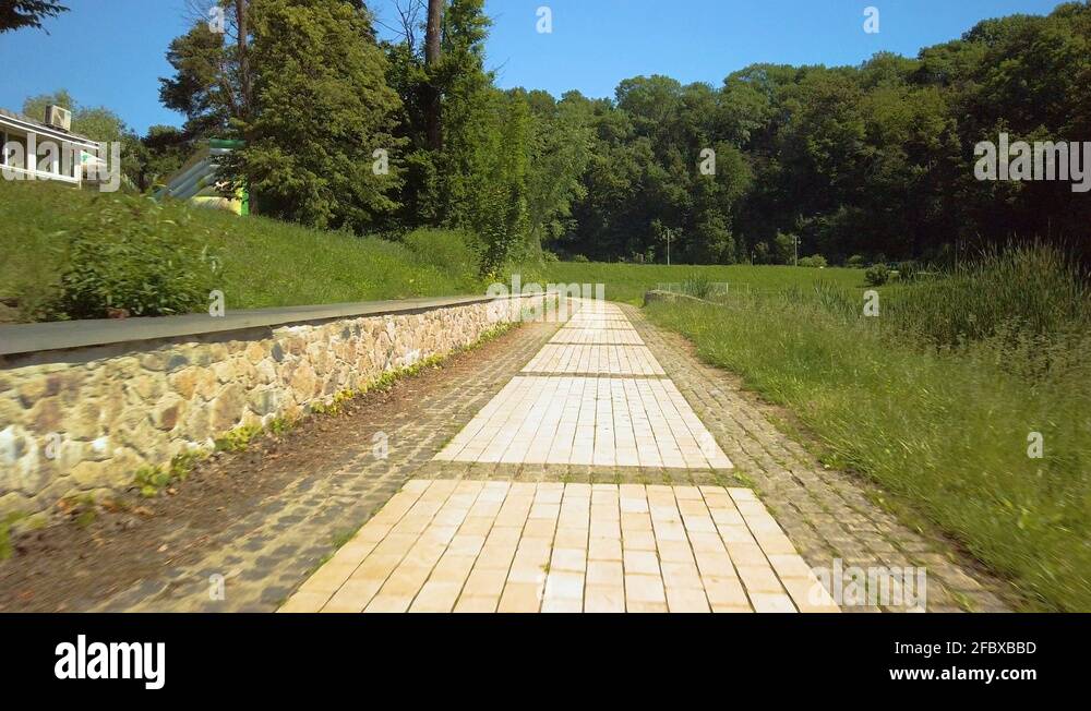 Low hovering shot along a pedestrian pathway in a park surrounded by ...