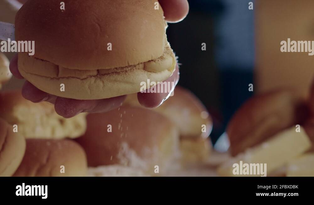 Close-up of chef's hand cutting burger bun in half with sharp knife. 4K ...