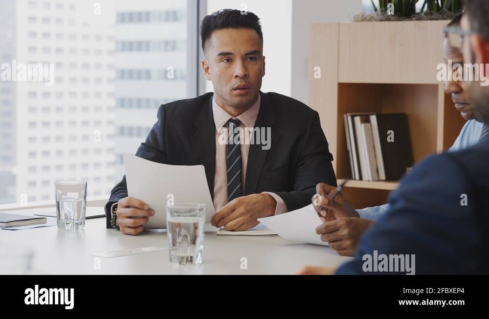 Three Businessmen Sitting Around Table Meeting In Modern Open Plan ...
