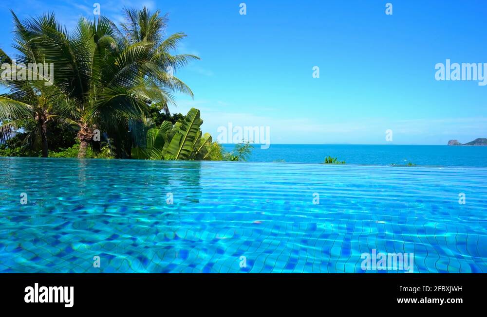 Static shot of an infinity pool with the ocean behind it and blue skies ...