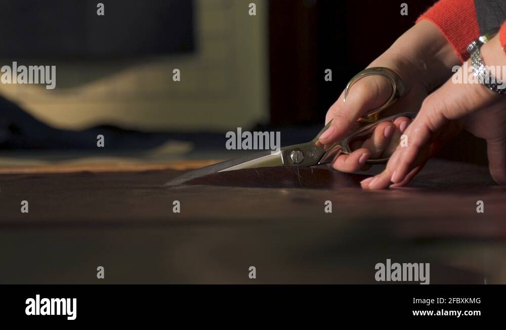 Women hands Cutting scissors cut the skin on the table, making leather ...