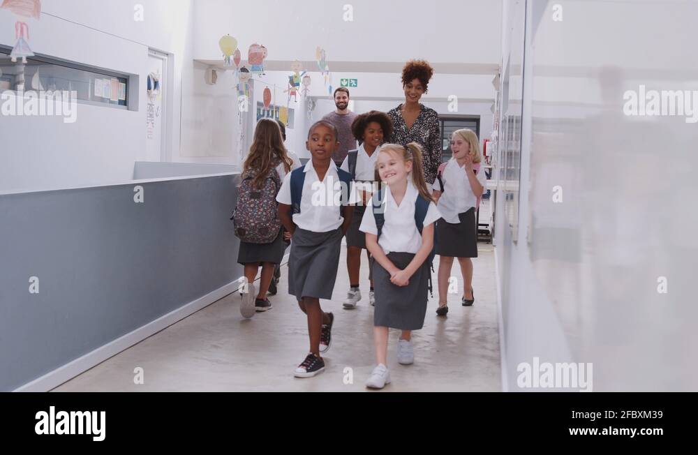 Teacher And Pupils Walking Along Corridor In Busy Elementary School ...