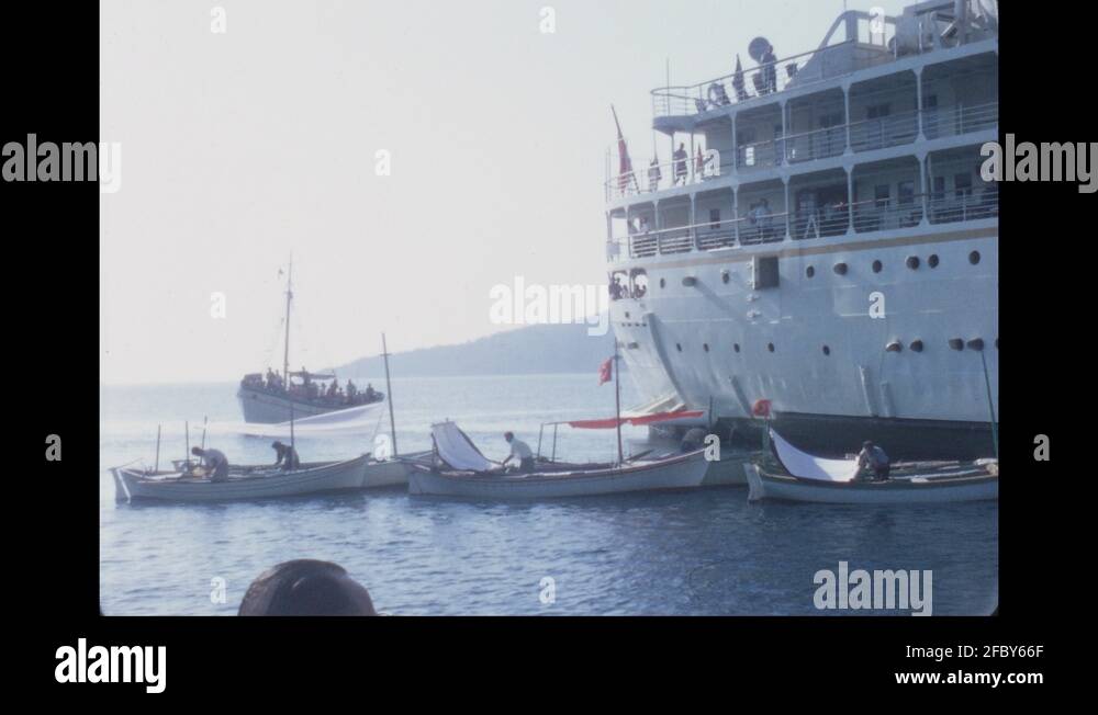 1950s: Small boats line up next to large boat. Boats travel across ...