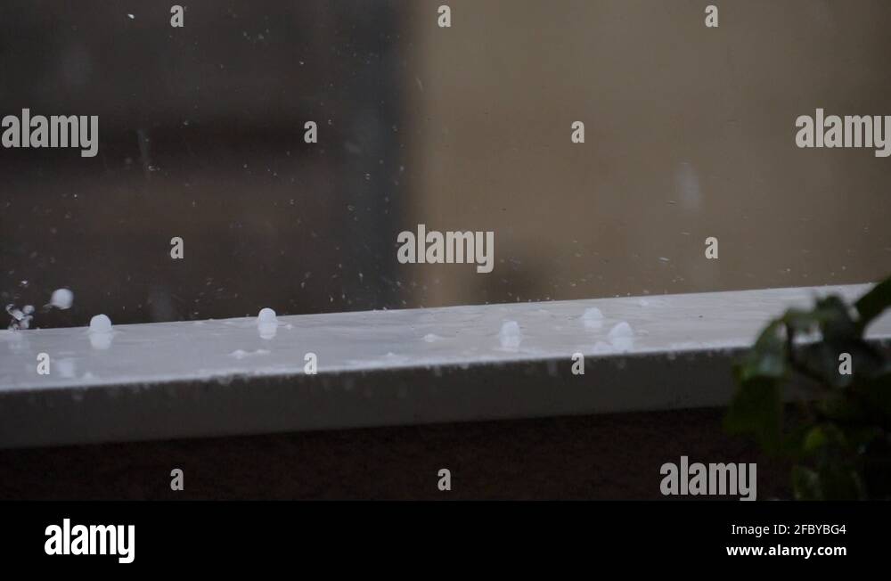 Hail drops splashing and rolling on a balcony railing during a storm at ...