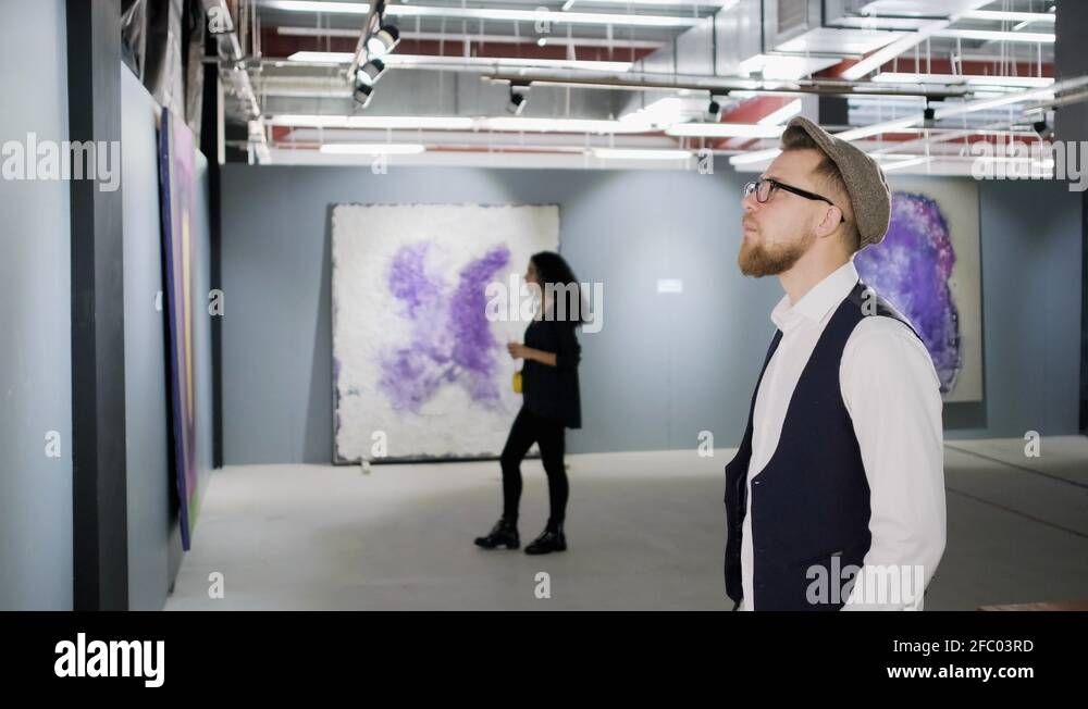 People are examining pictures in hall of modern art gallery, man and ...