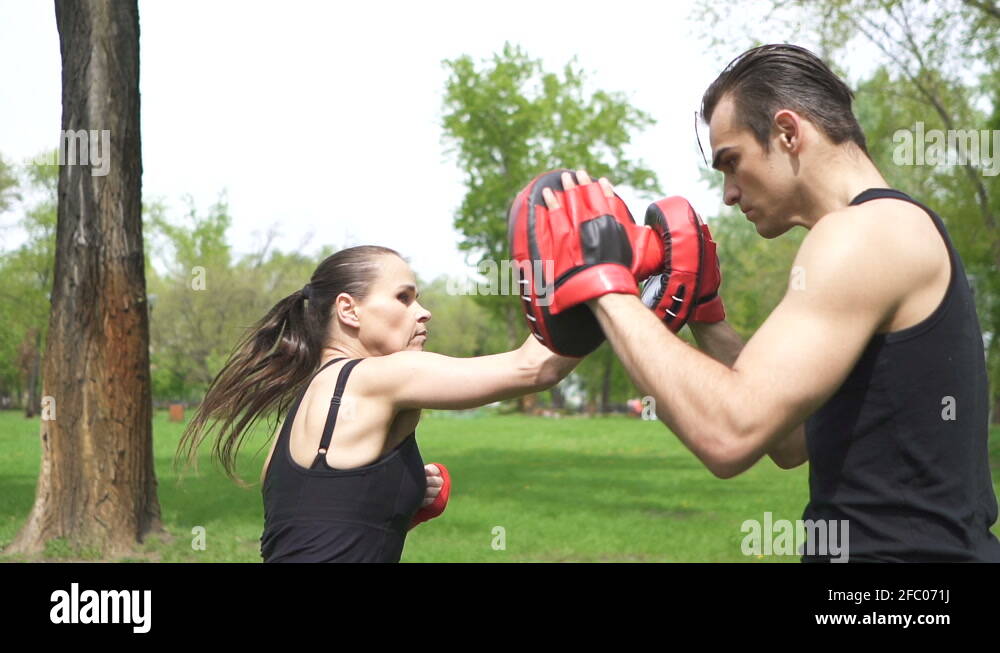 Muscular man training boxing process of woman in street park outdoor ...