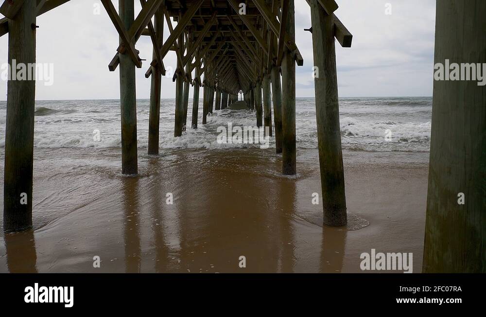 Looking under a beachfront pier as the waves roll in - slow motion ...