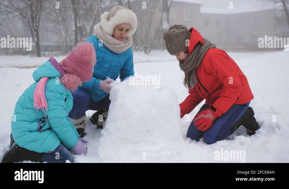 Parents and children playing in the snow. Mom and two daughters sculpts ...