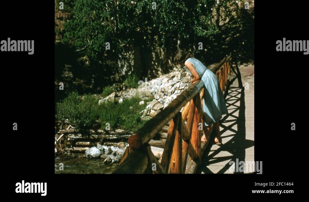 1950s: Woman leans over railing, looks at water under bridge. Waterfall ...