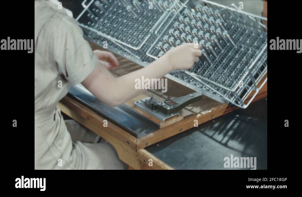 1950s: Woman at work station takes bullet shell casings from rack ...