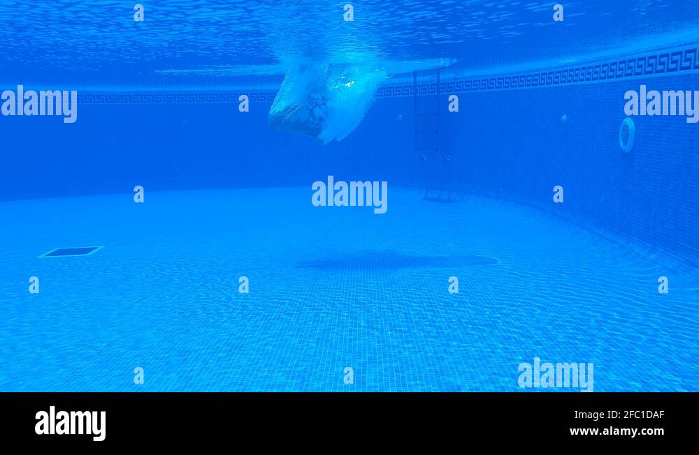 Underwater shooting as a man dives like a bomb into the pool and swims ...