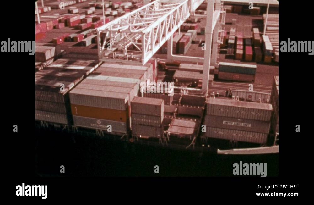 1970s: Aerial view of crane and cargo ship. Crane lifts shipping ...
