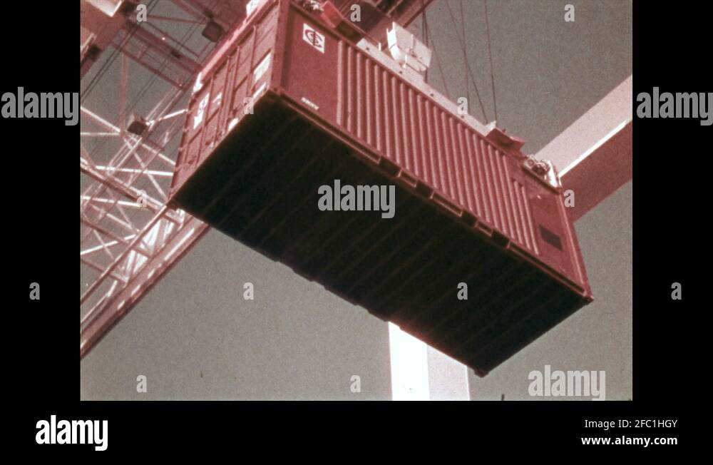 1970s: Crane lifts shipping container from cargo ship. Man directs ...