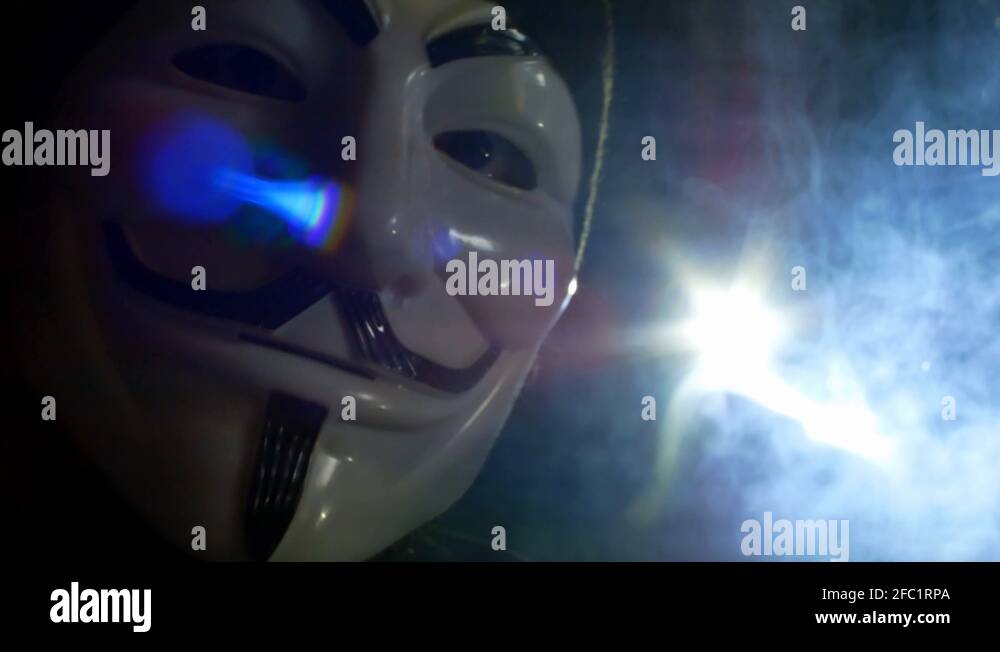 Man in anonymous mask backlit with spotlight in smoke background ...