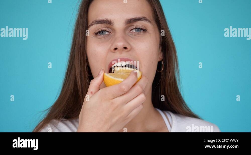 Young girl eats a lemon. Woman grimaces while eating a sour lemon Stock ...