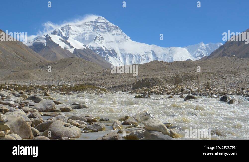 LOW ANGLE: Dirty stream flows across the rocky foothills of snowy Mount ...