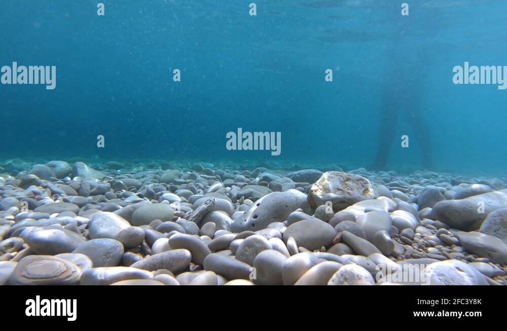 Underwater view of rocks falling into the sea with two people walking ...