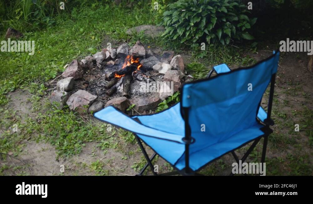 Campfire and burnig fire outdoors. Empty blue folding camp chair Stock ...