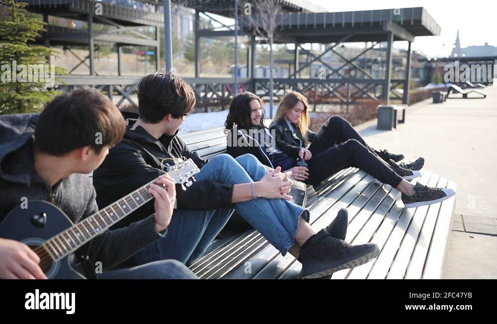 Young friends chilling on a bench - drinking alcohol and playing the ...