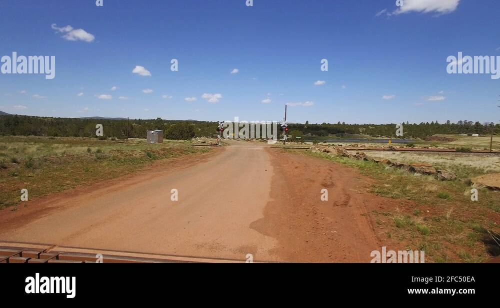 An aerial of dirt road crosses over railroad track warning lights are ...