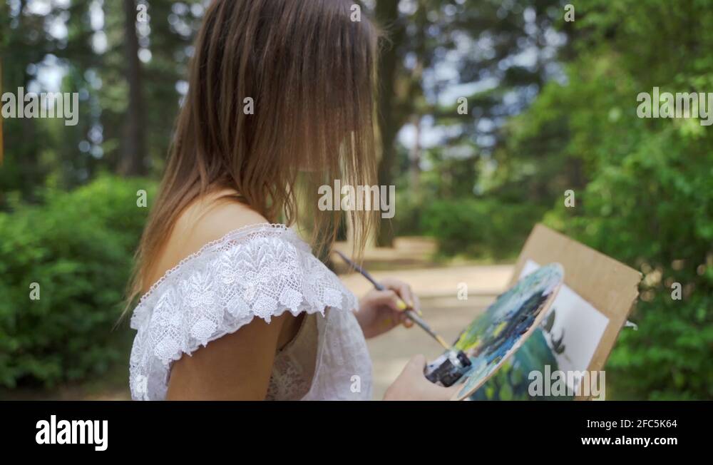 Girl artist in the park paints a landscape with oil paints a small old ...