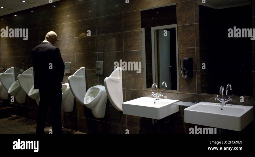 Bald man businessman in suit in between work pees in urinal in public ...