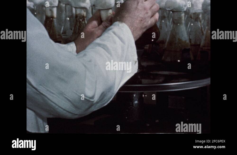 1950s: Man removes beakers from machine. Man pours liquid into vessel ...