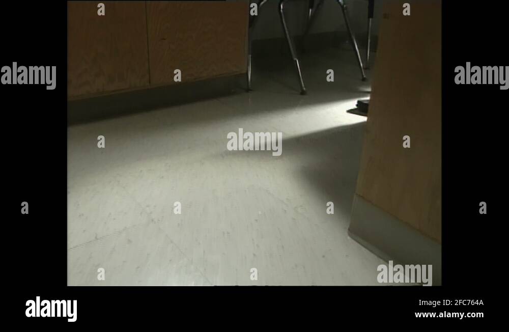 1990s: Feet of teacher walking across classroom. Three students stand ...