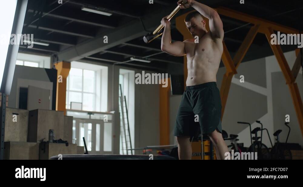 Muscular man hits a tire with a sledgehammer, crossfit training with ...