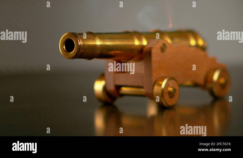 MACRO, DOF: Miniature golden cannon emits white smoke before firing a ...