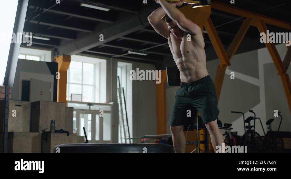 Muscular man hits a tire with a sledgehammer, crossfit training with ...