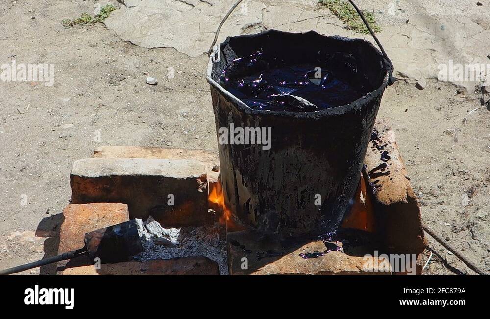 A bucket of boiling resin on bricks. Pieces of bitumen are melted in a ...