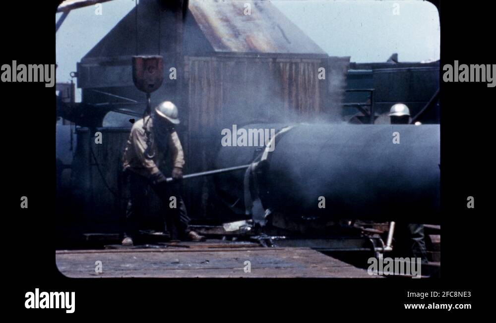 1940s: UNITED STATES: man cuts section of pipe. Pipe in machine. Men ...