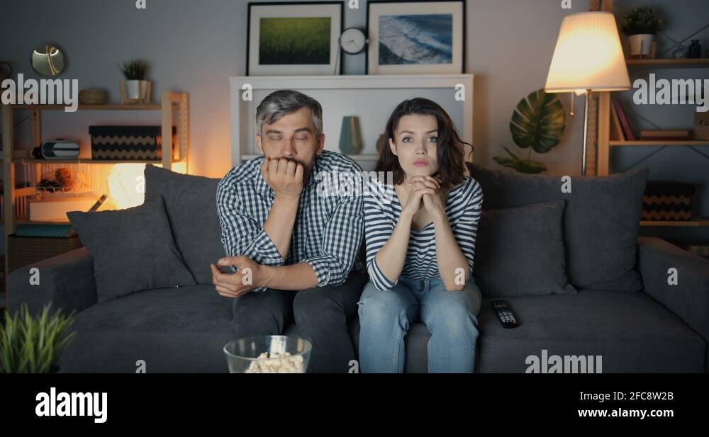 Shocked girl and guy watching TV with serious faces touching face at ...