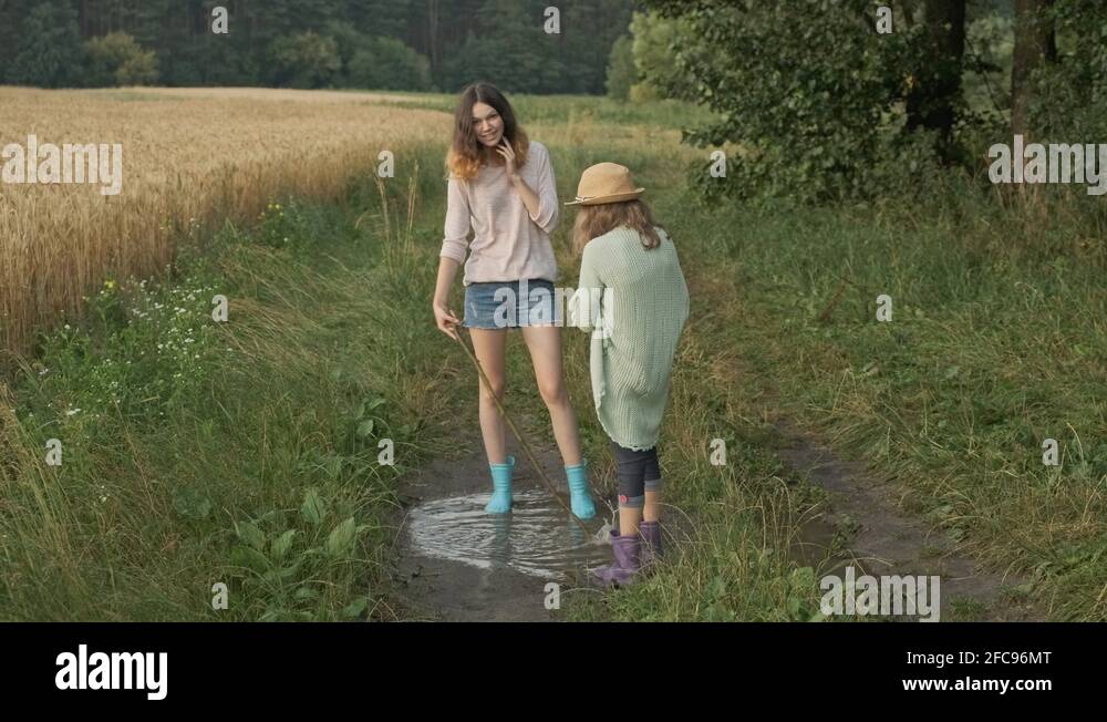 Two happy girls sisters in boots playing in puddle of rainwater Stock ...