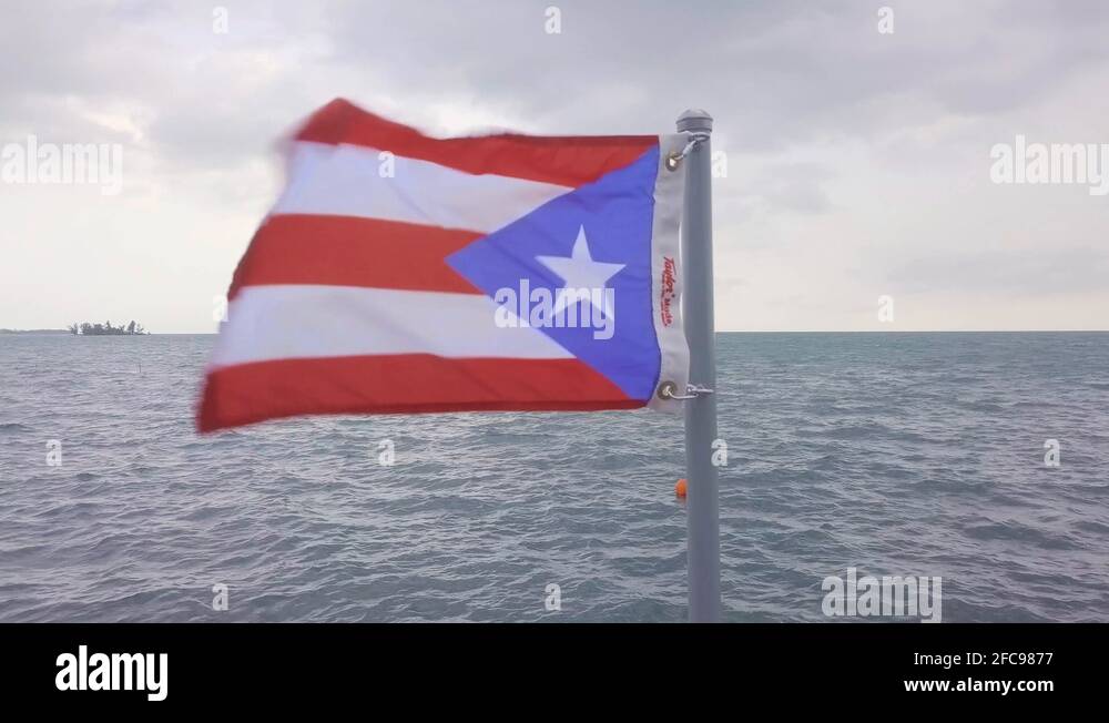 cinematic footage of Puerto Rican flag blown by the wind behind the sea ...