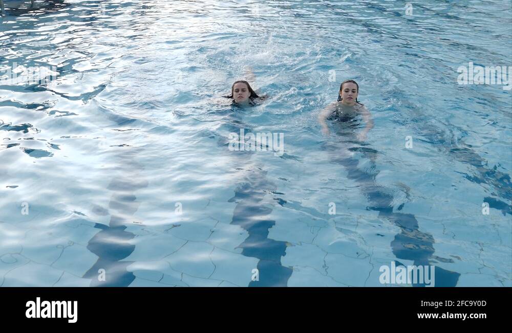 Two young girls swim in the pool with glare of the sun on the water ...