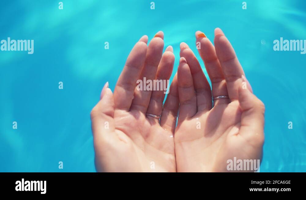 Tan hand of a young girl pouring water in her palms from a blue pool ...