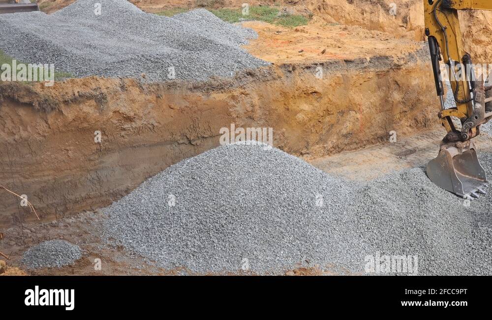 Excavator bucket backfilling trench for stone backfill of foundation ...