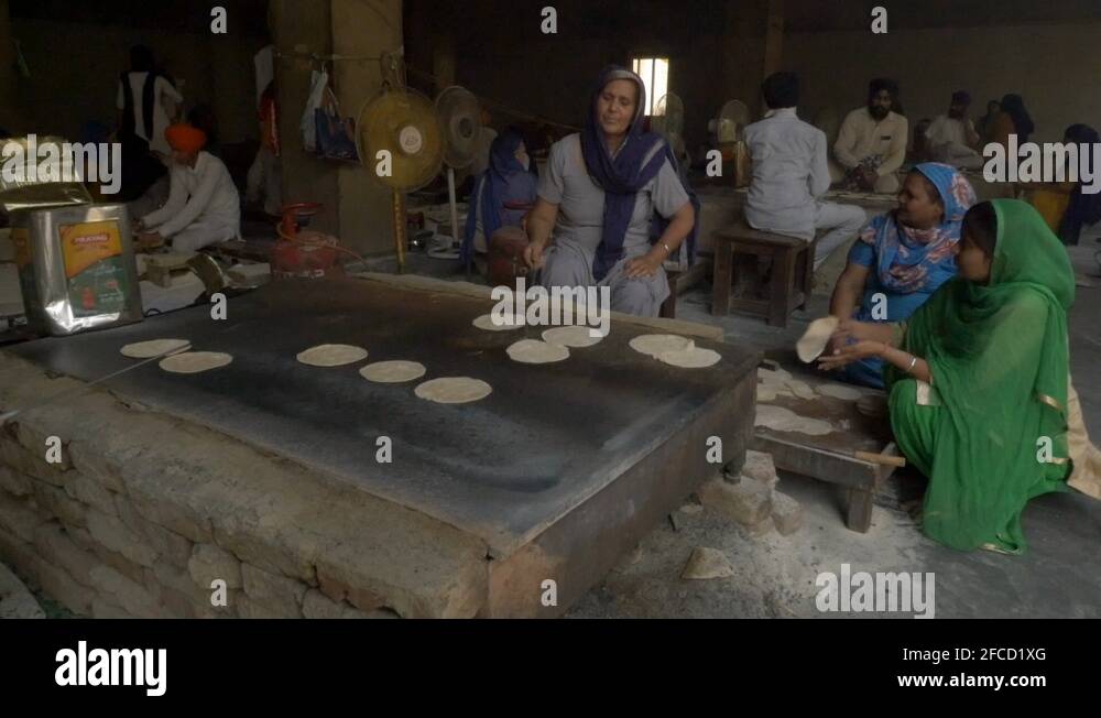 Women cooking flattened bread, called roti, on a flat top grill in the ...