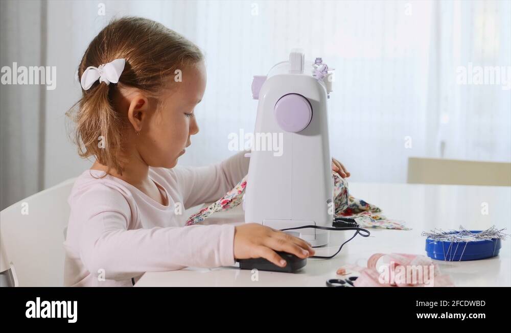 A little girl is sewing. A child is stiching fabric. Side viw, close-up ...