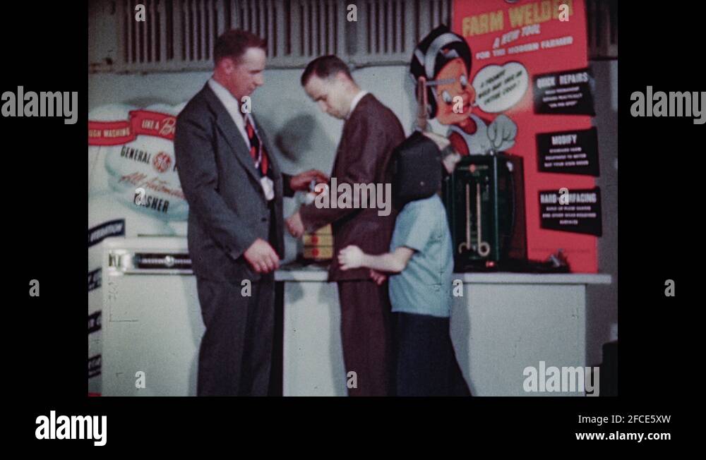 1940s: UNITED STATES: man talks to welding salesman. Boy tries on ...