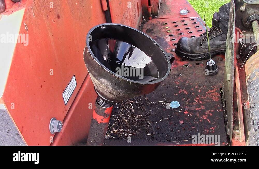 Pouring oil from a five gallon pail into a funnel to fill a hydraulic ...