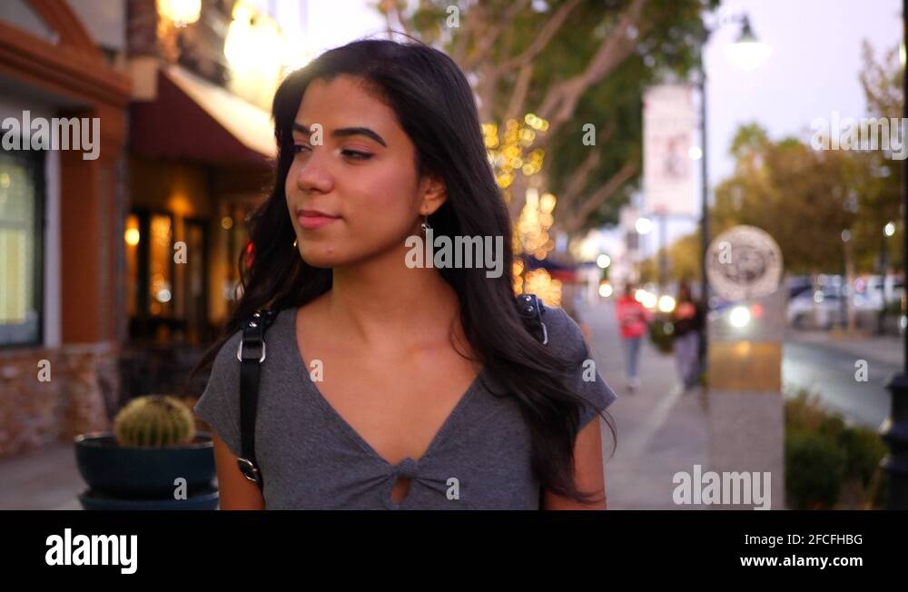 A beautiful hispanic woman walking a downtown urban city street looking ...