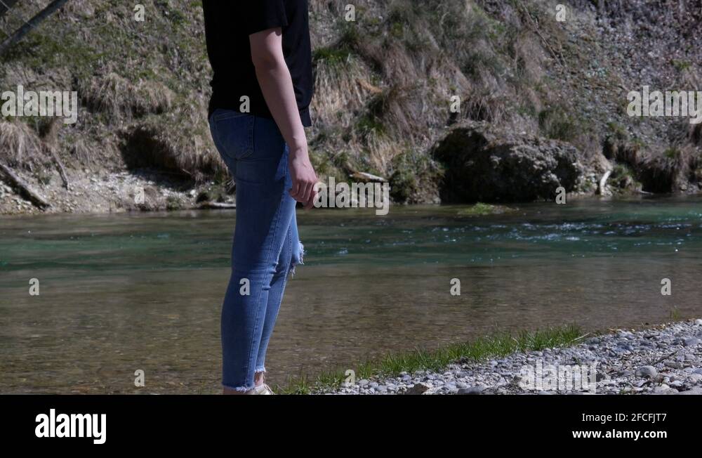 Tall woman throws a rock in shallow flowing river and gives a thumbs up ...