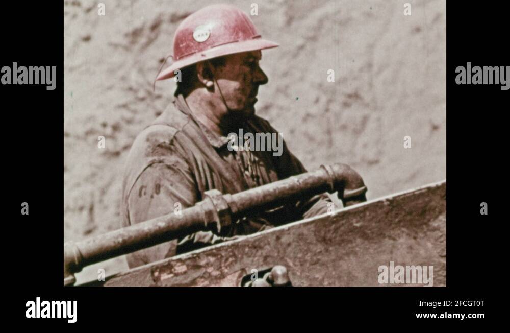 1950s: Man works machine in rock quarry. Men stand around vehicles in ...