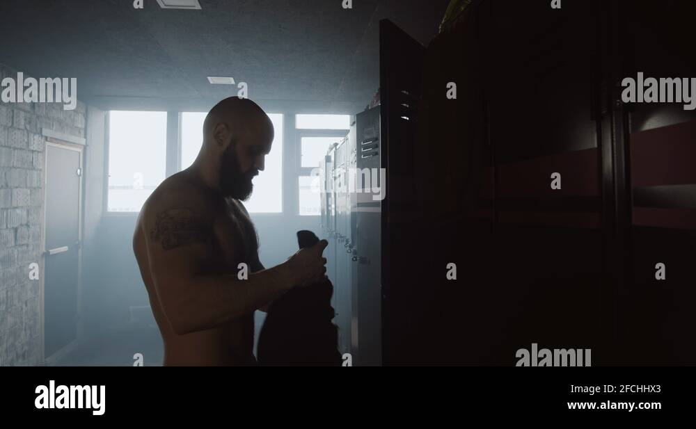 Exhausted young shirtless man sitting alone in dark gym locker room ...