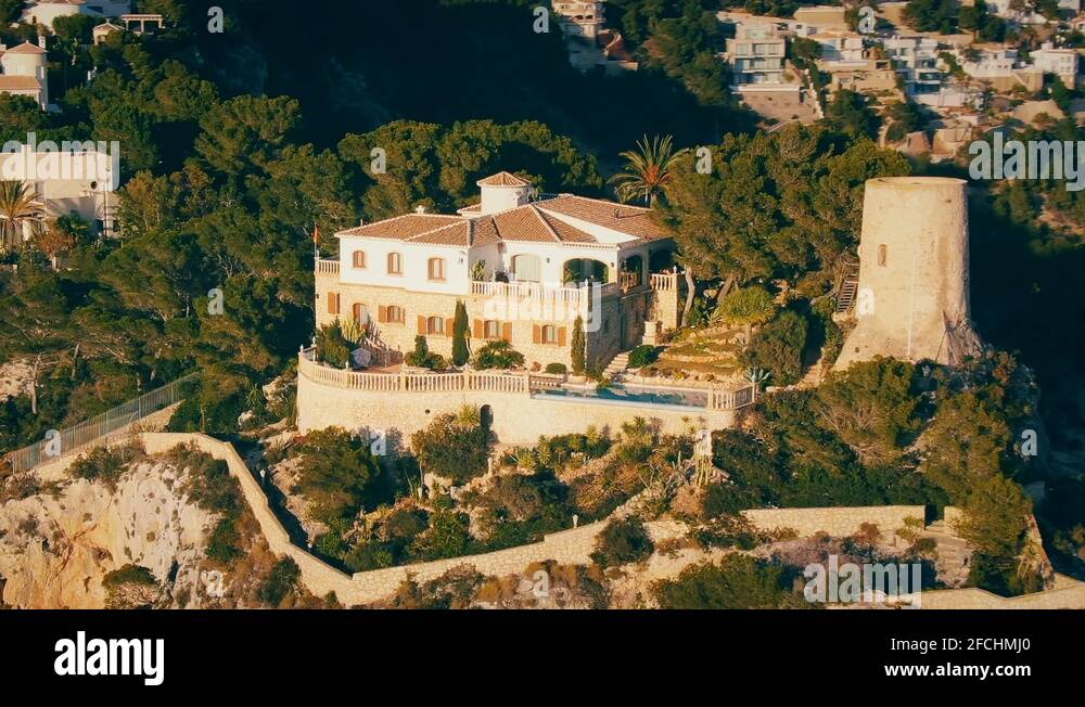 Big mansion near ocean, built on top of rock cliff with trees and palms ...